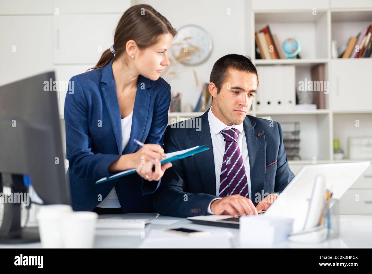 Female assistant writing down tasks on clipboard near boss Stock Photo ...