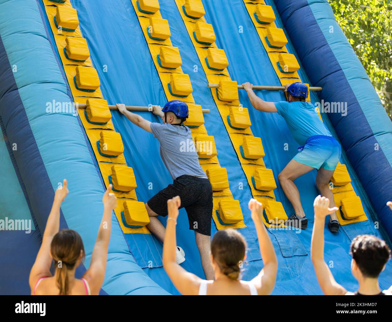 Two male friends climbing on inflatable slide with wooden poles Stock ...