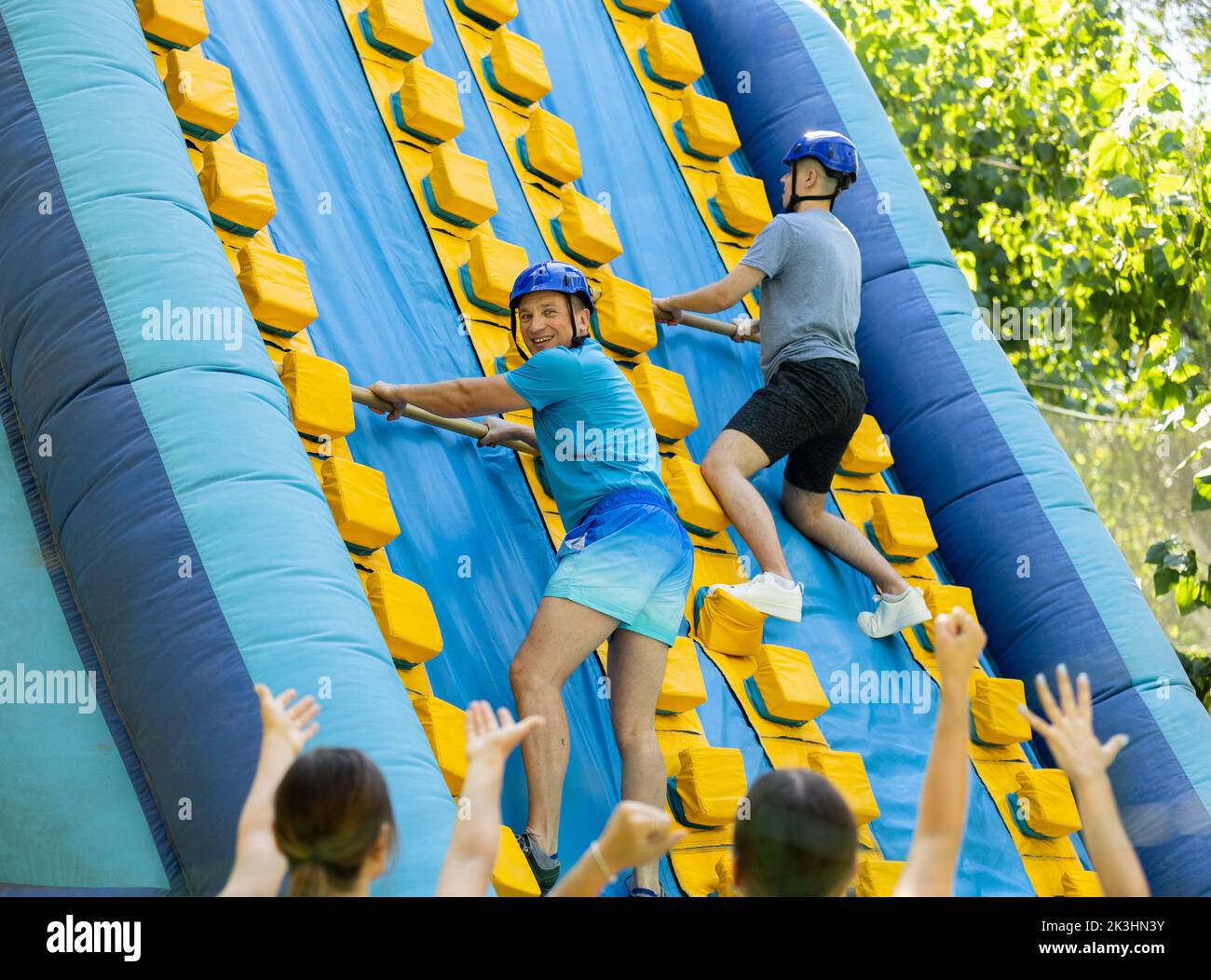 Cheerful man climbing on inflatable slide with wooden poles Stock Photo ...