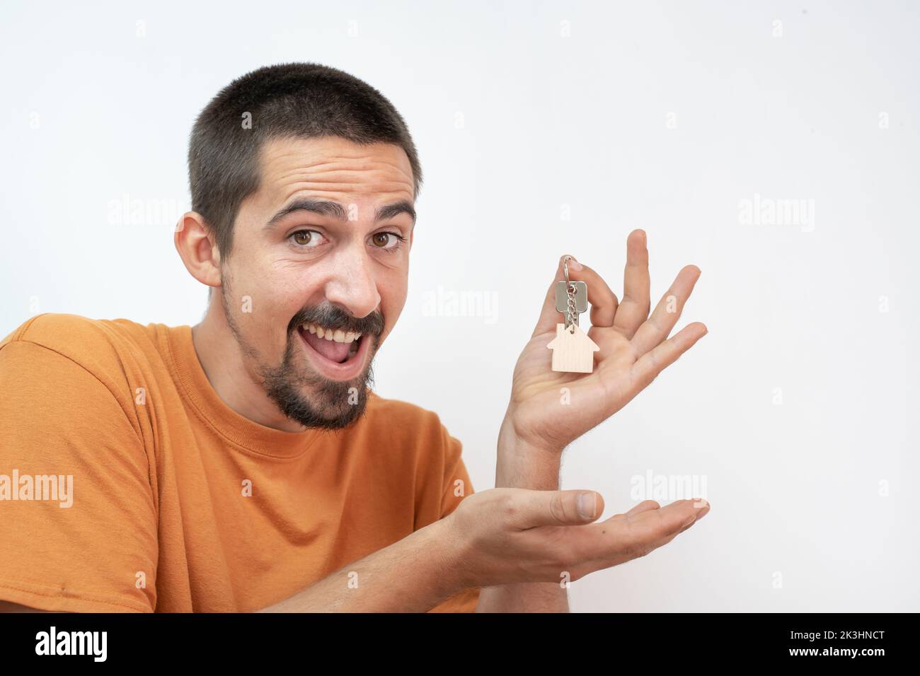 Happy young man smiling with the new home keys. Keychain in the shape ...