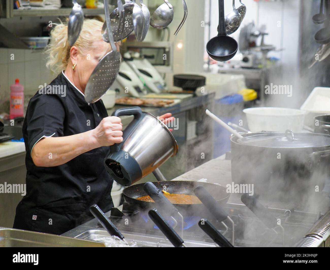 chef in white uniform pouring boiled spaghetti into pan wok for cooking ...