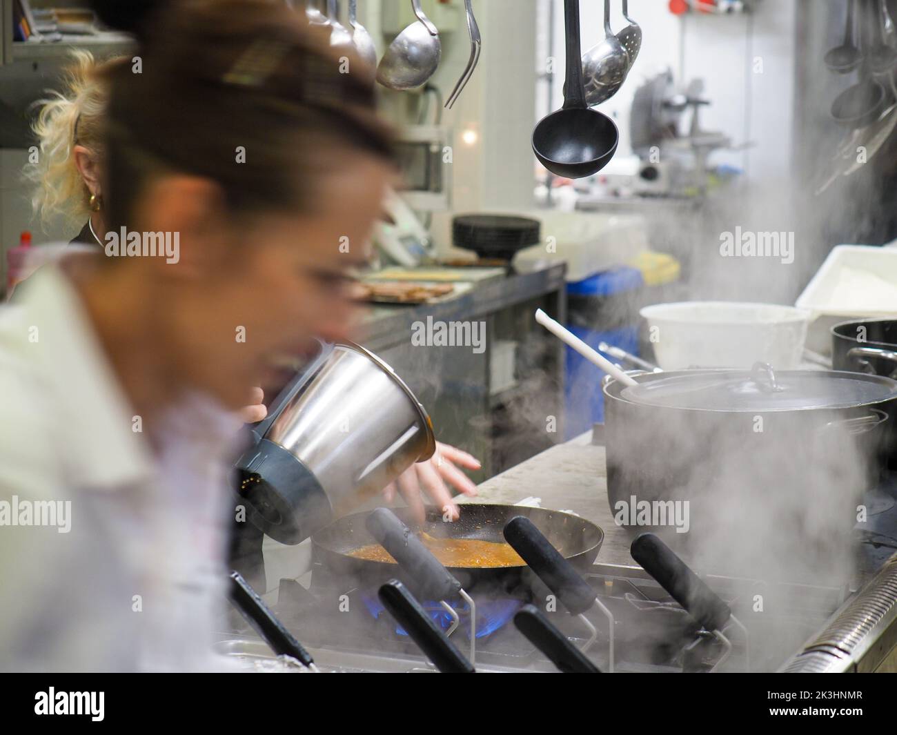 chef in white uniform pouring boiled spaghetti into pan wok for cooking ...