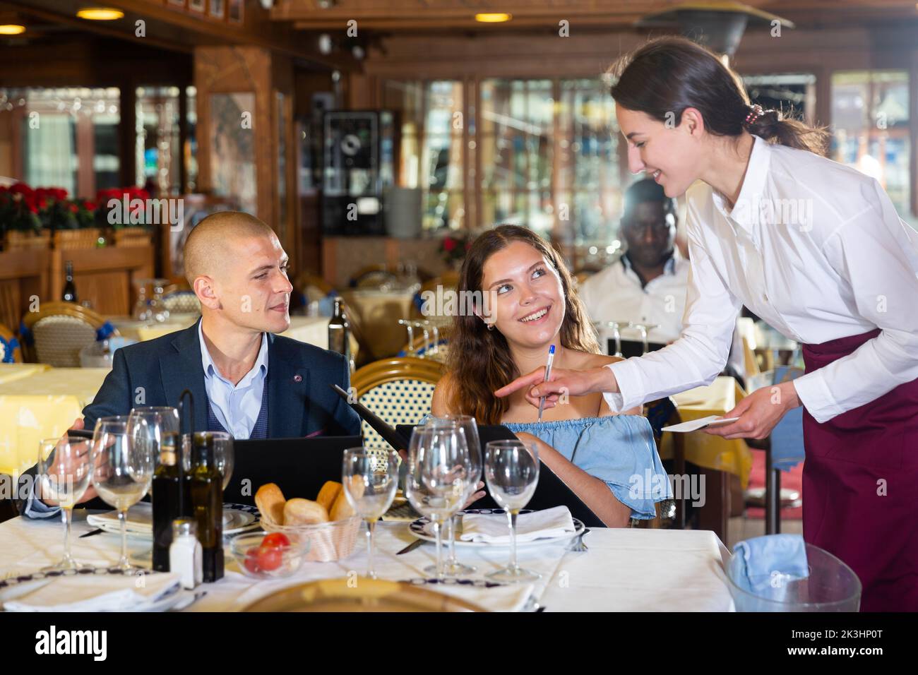 Young positive waitress taking table order from guests Stock Photo - Alamy