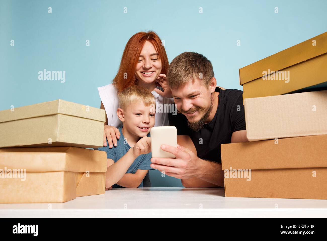 Happy family, parents and kid among cardboard boxes using smartphone ...