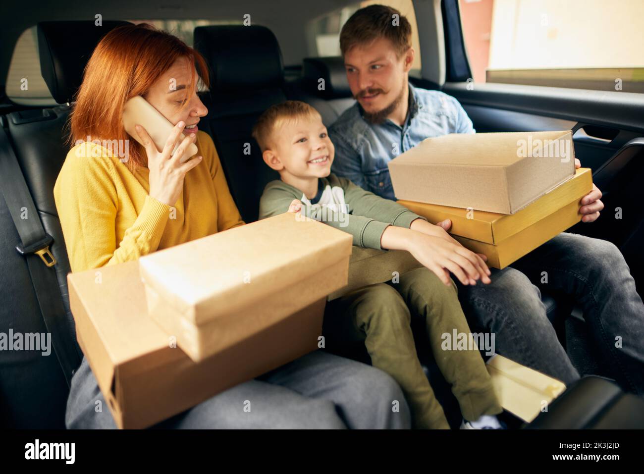 Young happy family, parents and kid sitting at car with a lot of carton ...