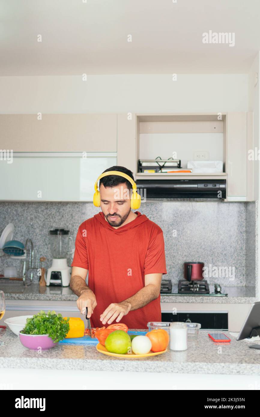 Portrait of a happy young man cooking while listening to music with ...