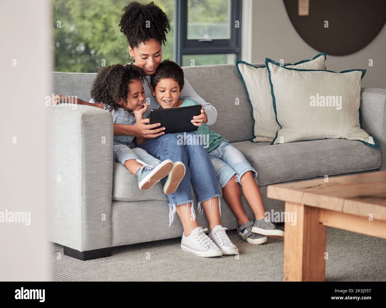 A mother with children on couch with tablet to watch educational shows ...