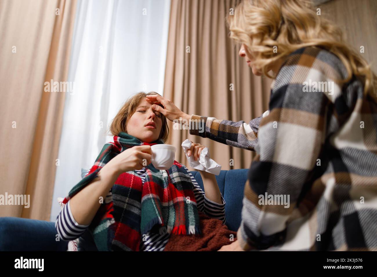 Girl with the flu drinks hot tea while her mother checks her forehead ...