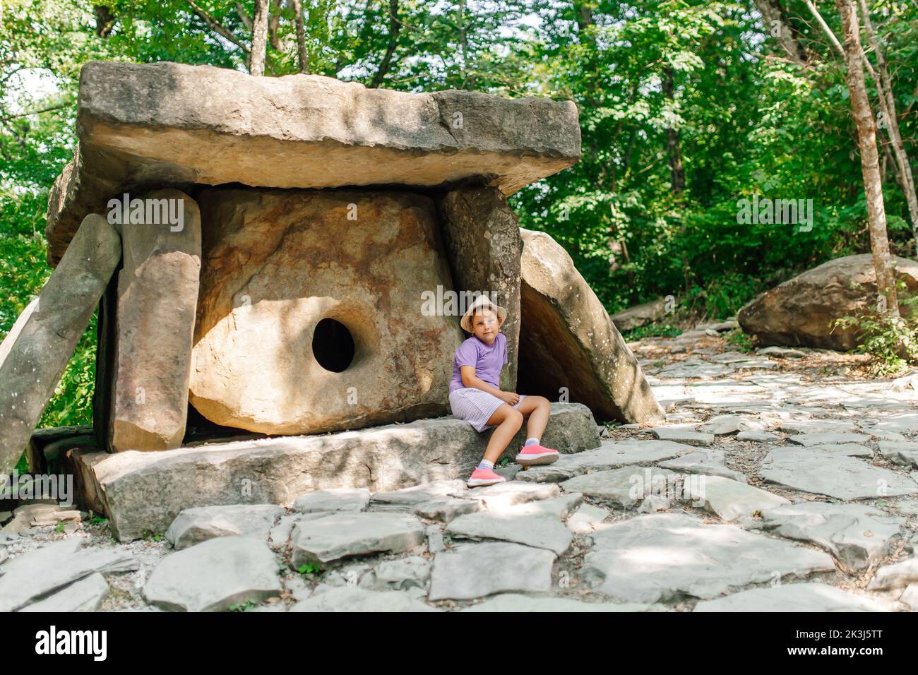 Little girl sit near ancient dolmen in green park on sunny day ...