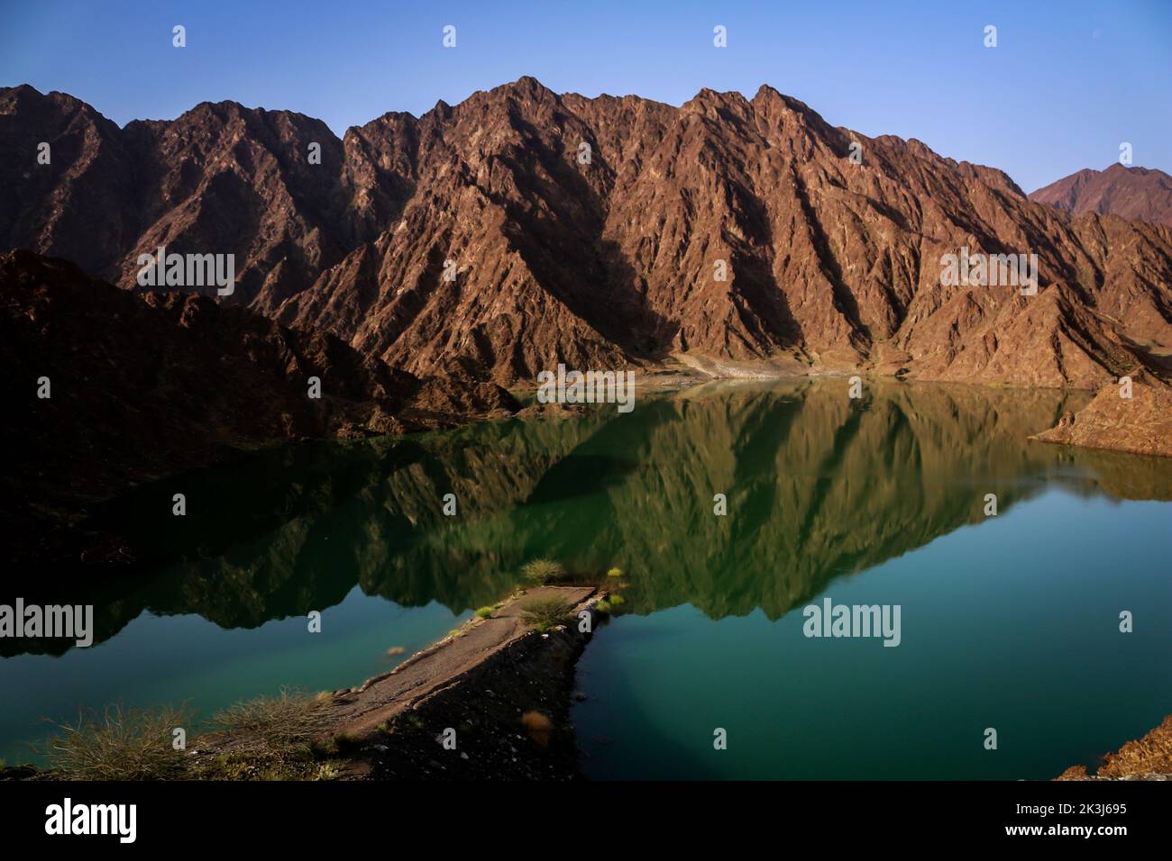 Beautiful deep green Hatta lake with rocky Hajar Mountains on ...