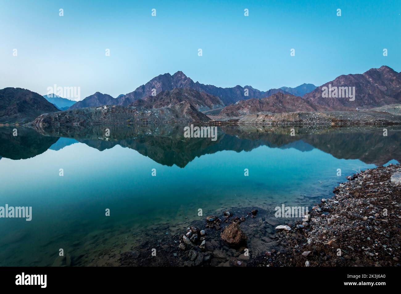 Beautiful deep green Hatta lake with rocky Hajar Mountains on ...