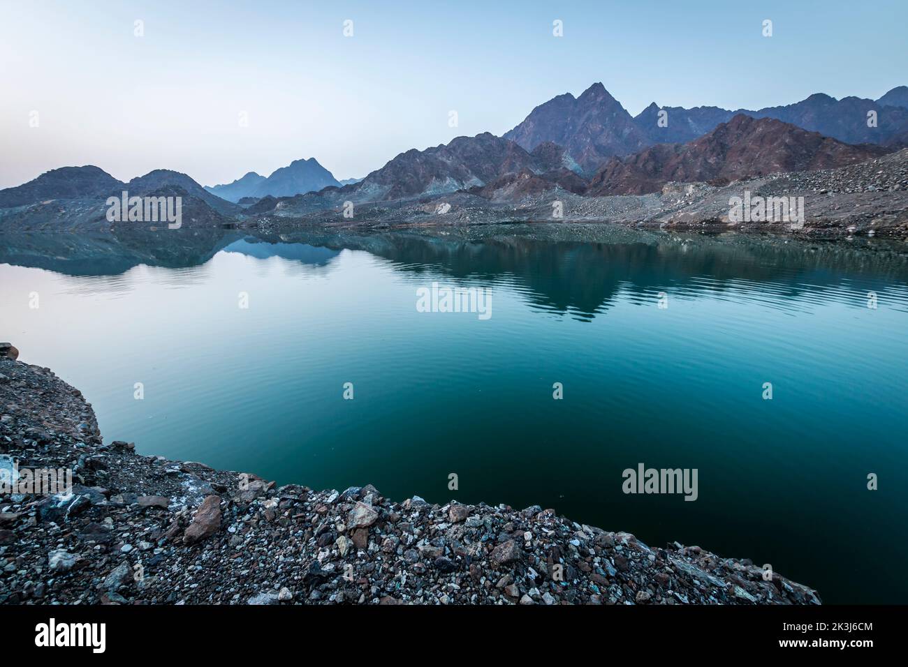 Beautiful deep green Hatta lake with rocky Hajar Mountains on ...