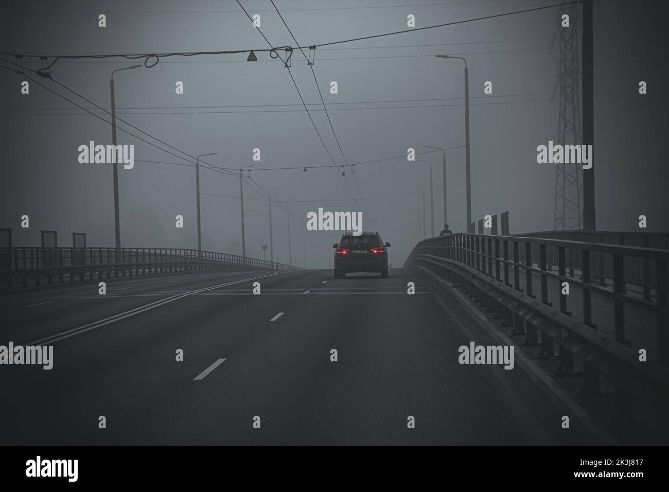 A car with red tail lights driving on a bridge in a very foggy and dark ...