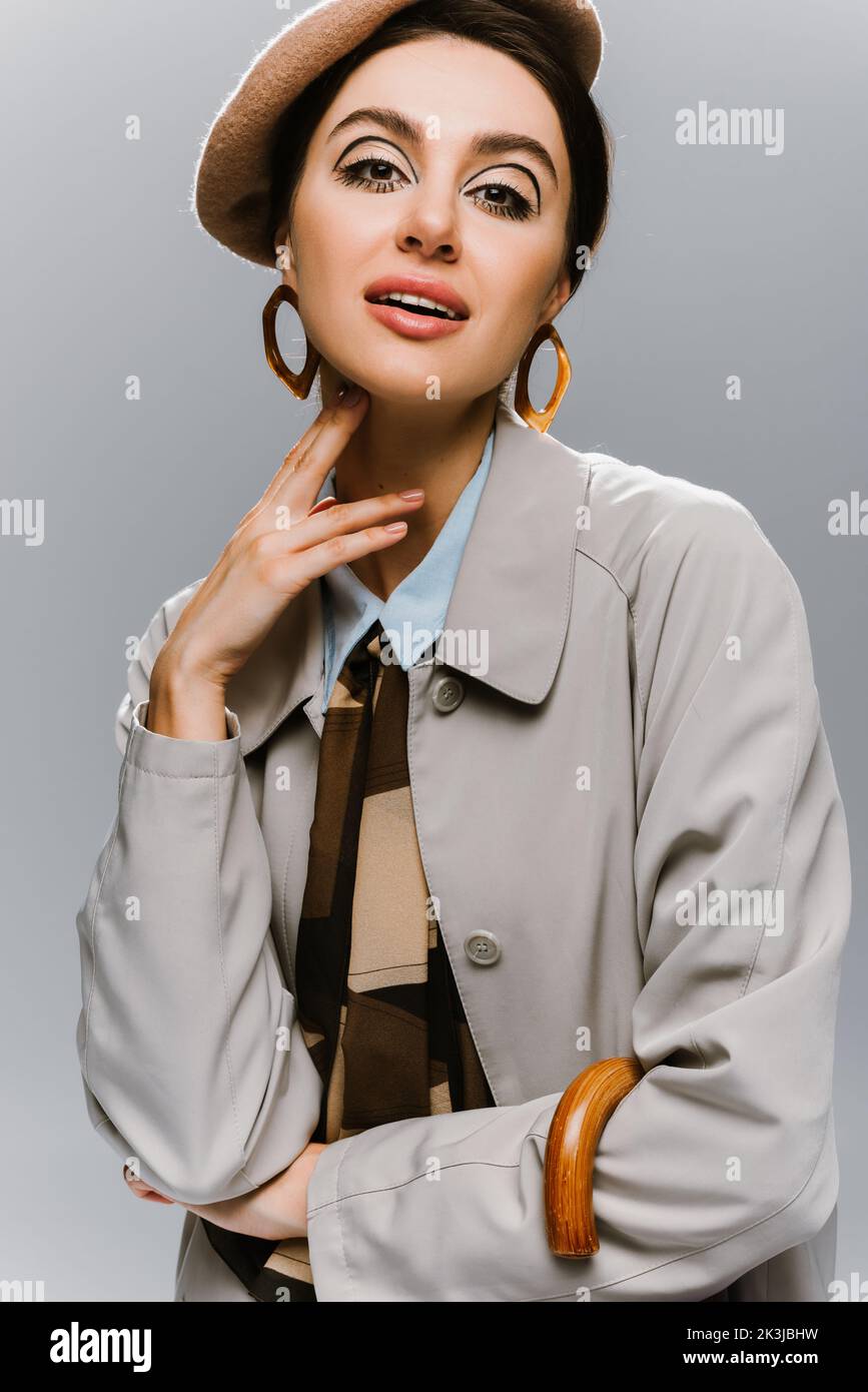 portrait of pin up young woman in beret and trench coat posing isolated ...