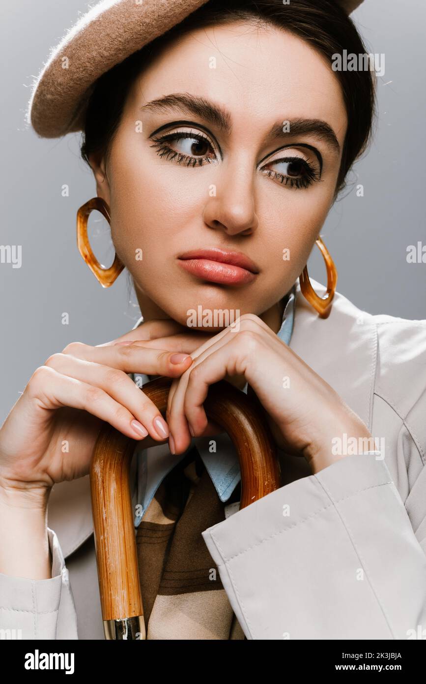 portrait of sad young woman in beret and trench coat posing with ...