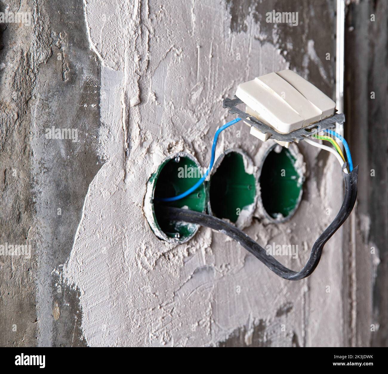 An electric switch hangs on wires from socket boxes built into a ...