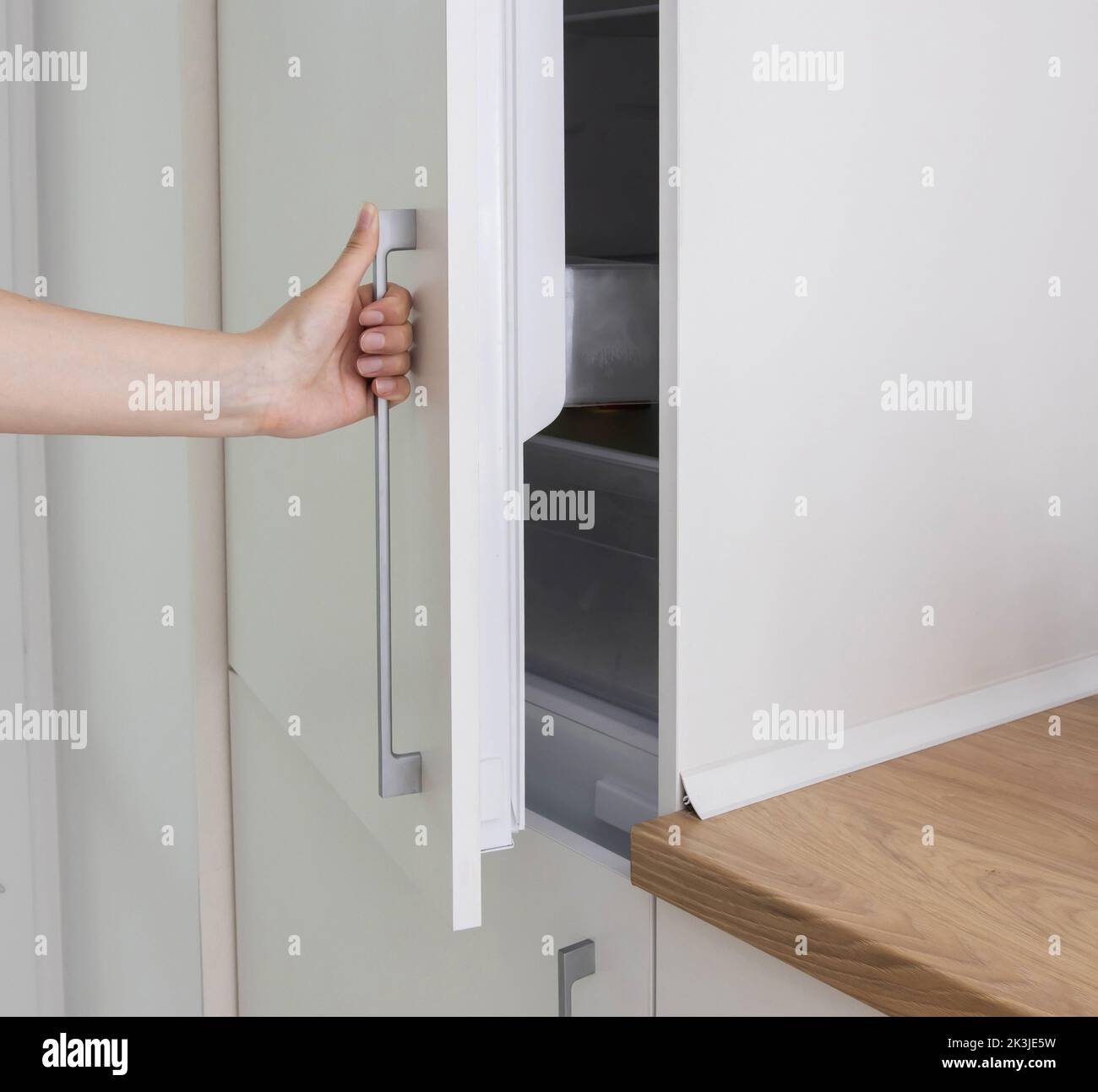 A man opens the door of a built-in refrigerator in the kitchen. Modern ...