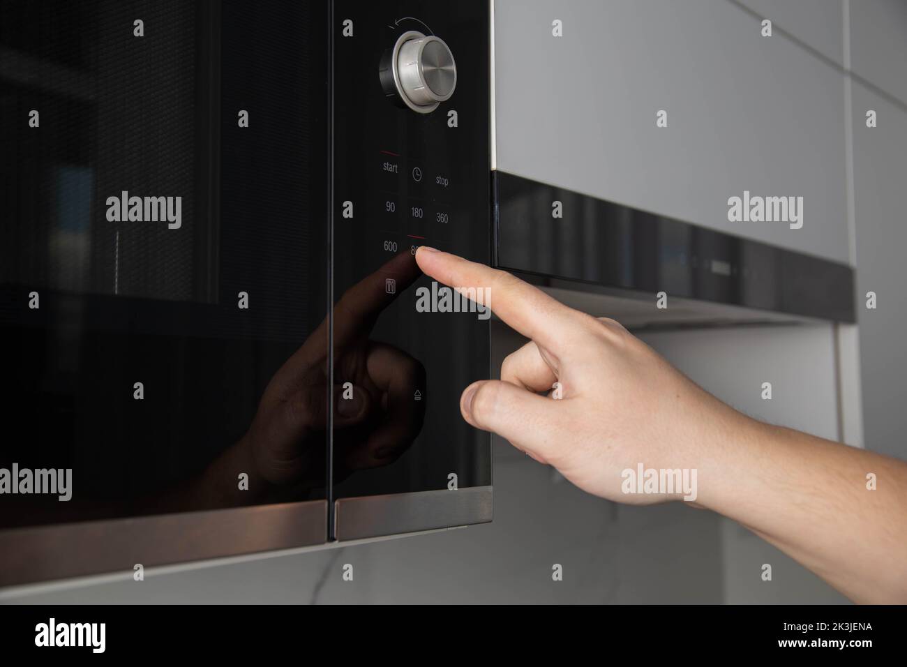 A man presses his finger on the touch panel of a microwave oven to turn ...