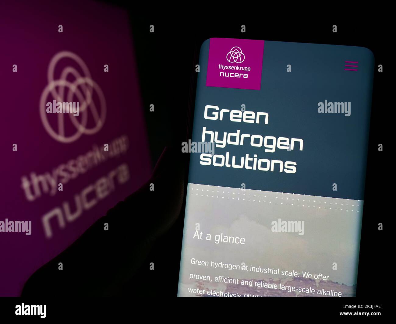 Person holding smartphone with webpage of company thyssenkrupp nucera ...