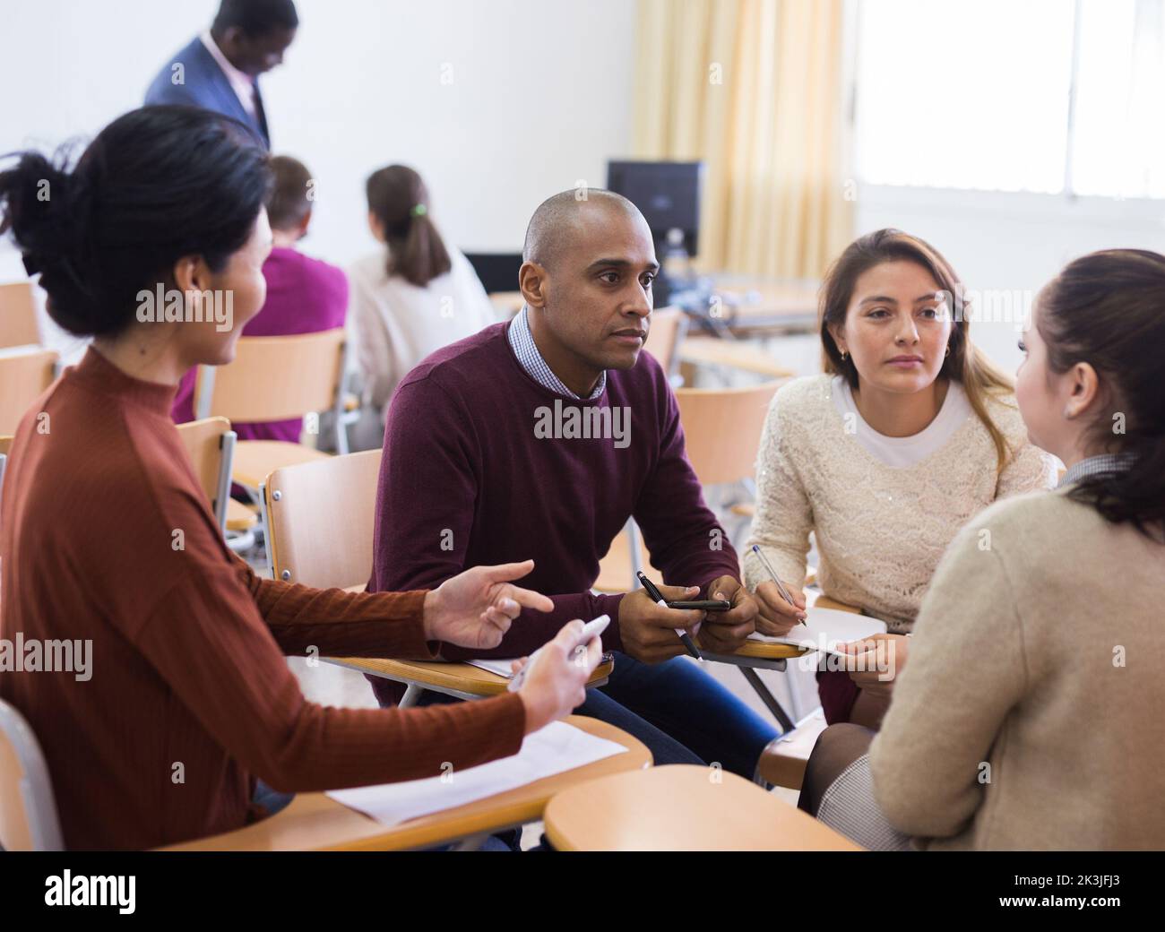 Positive students are talking about homework at desk Stock Photo - Alamy