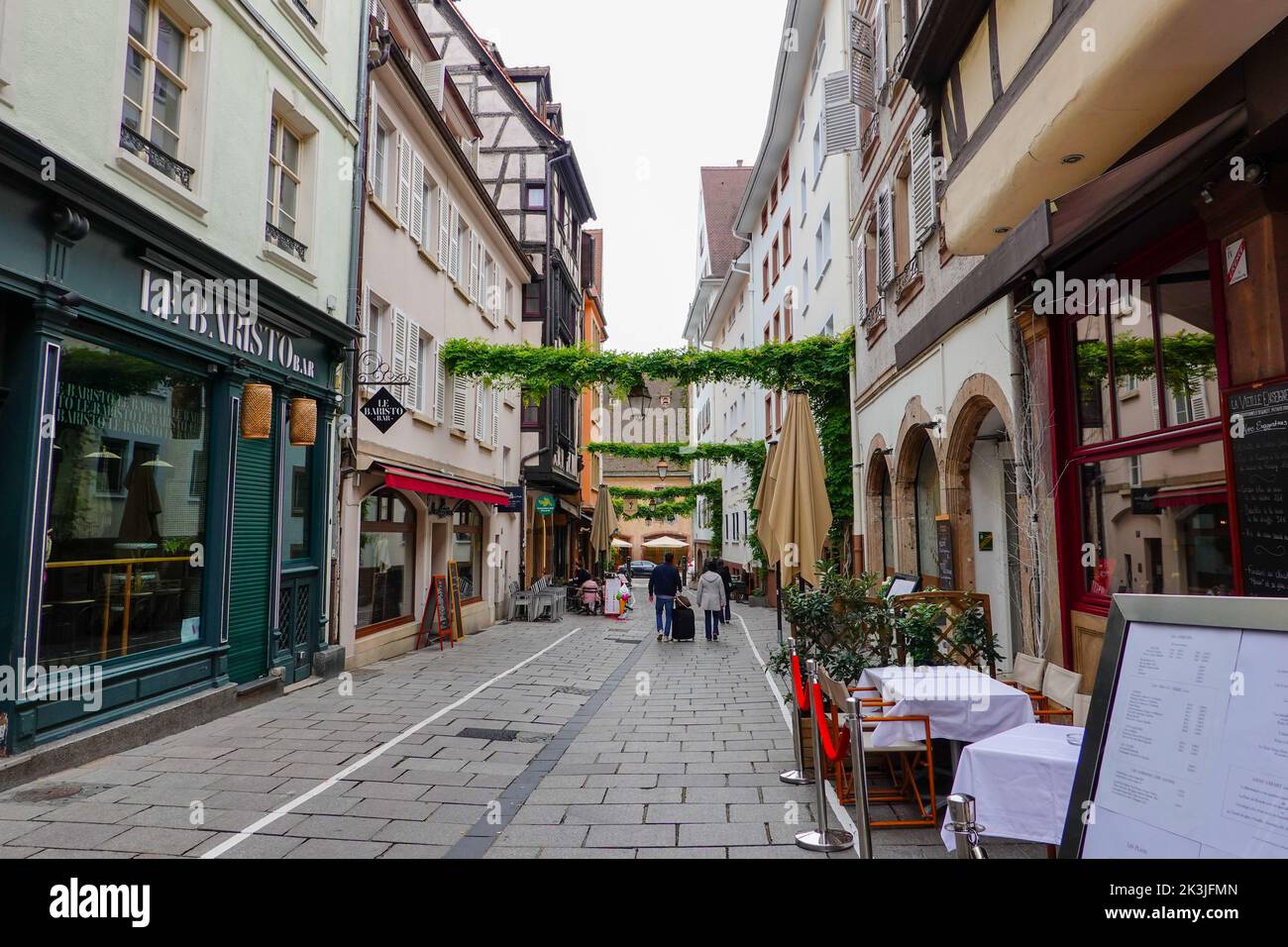 People, wheeling suitcase, through a narrow pedestrianized street, past ...