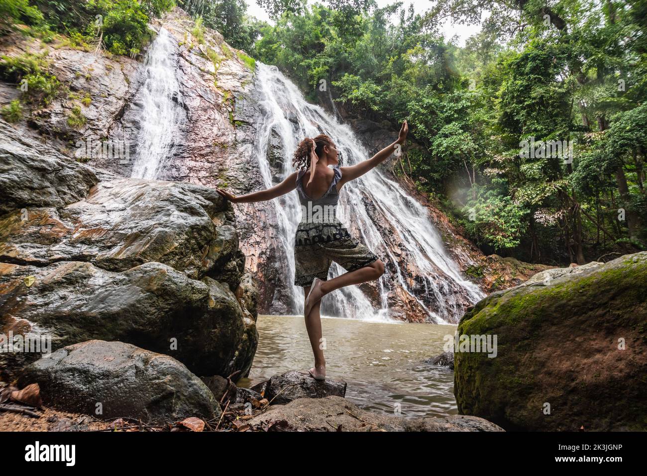 Woman doing yoga posture in front of a waterfall surrounded by ...