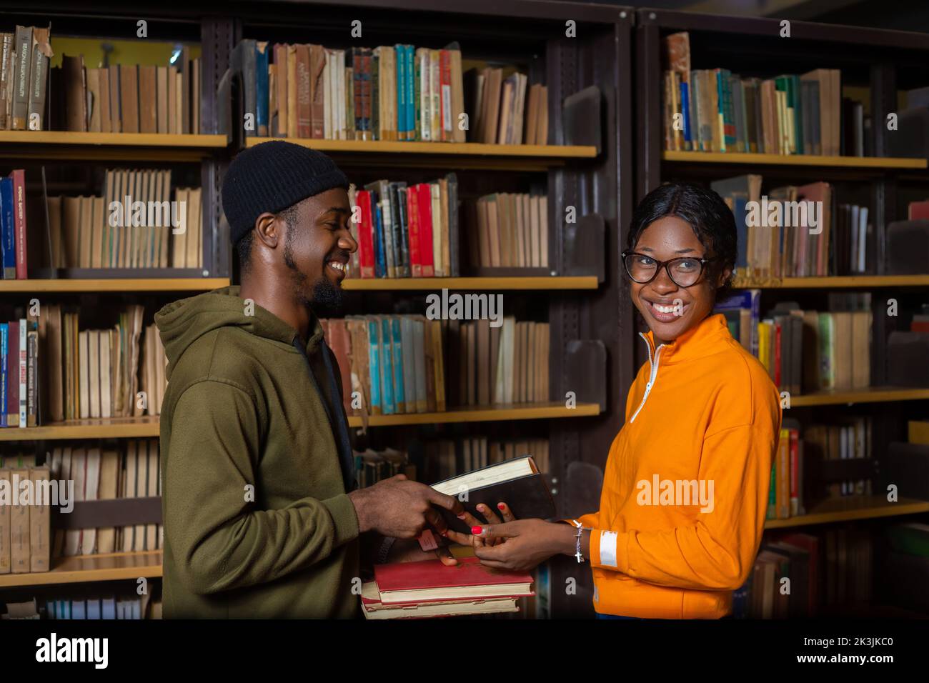 Two cheerful African American students exchanging books at a library ...