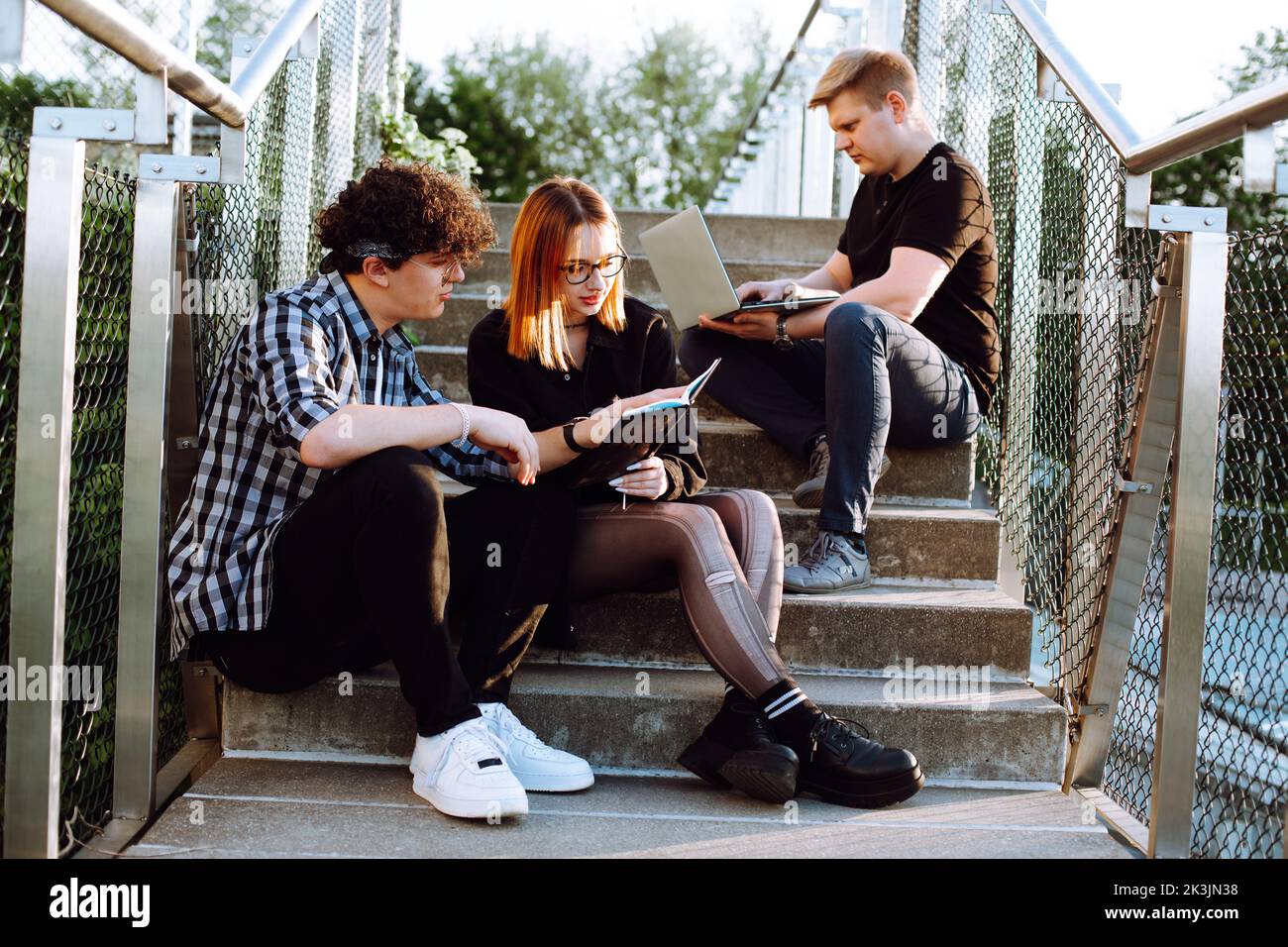 Mixed Group of three young students sitting studying together using laptop on university campus ...