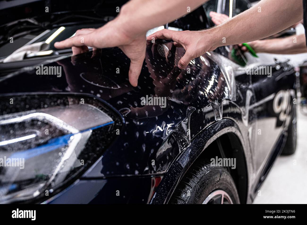 employee of the car detailing studio protects the fender of the car ...