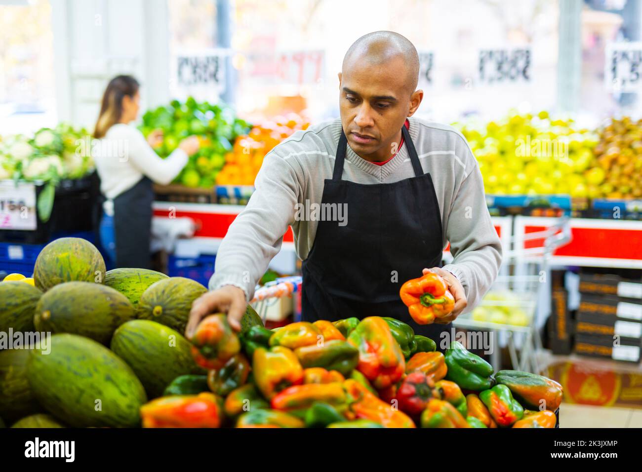 Supermarket worker in black apron putting vegetables Stock Photo - Alamy