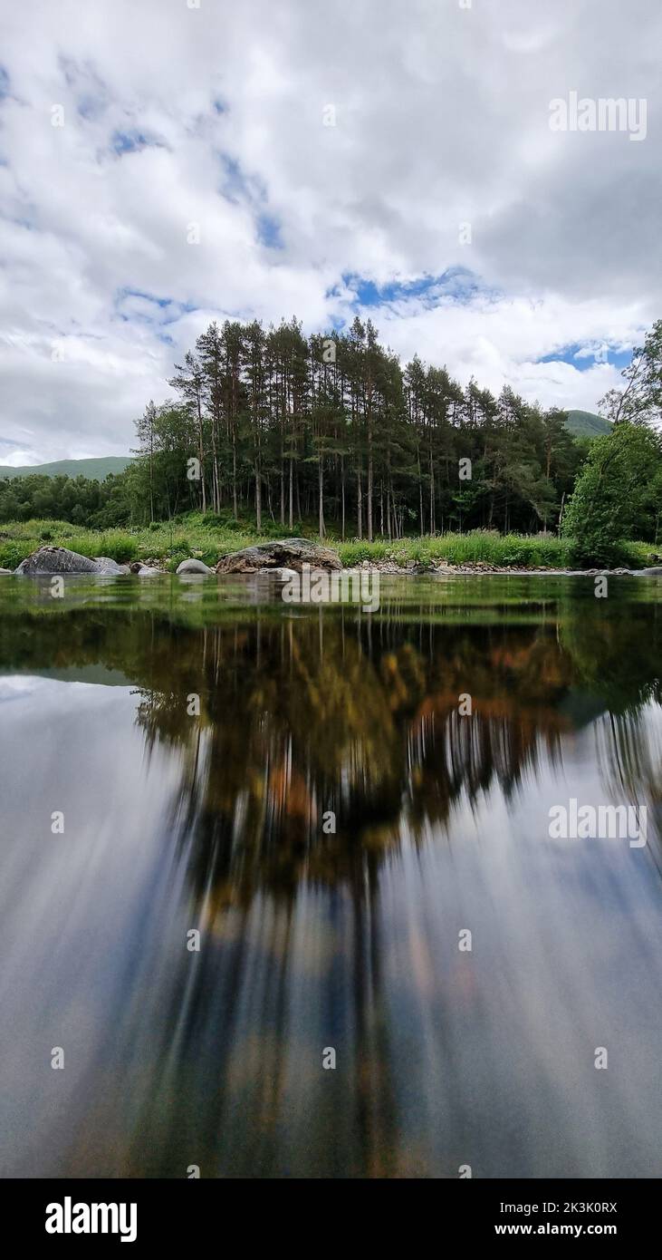 A vertical of a beautiful mirror lake with a reflection of trees by the ...
