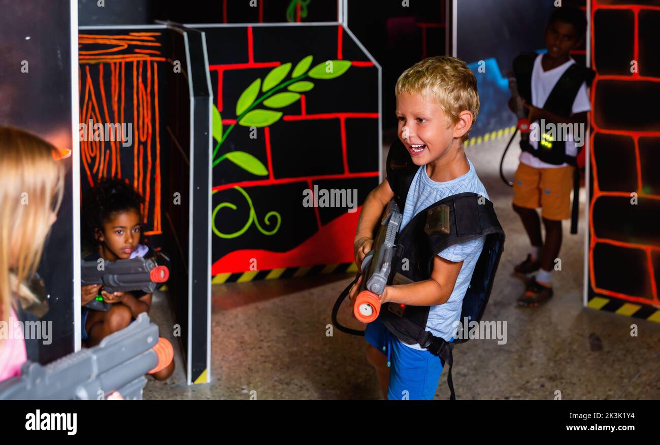 Multiracial team of happy tween kids aiming laser guns at other players ...