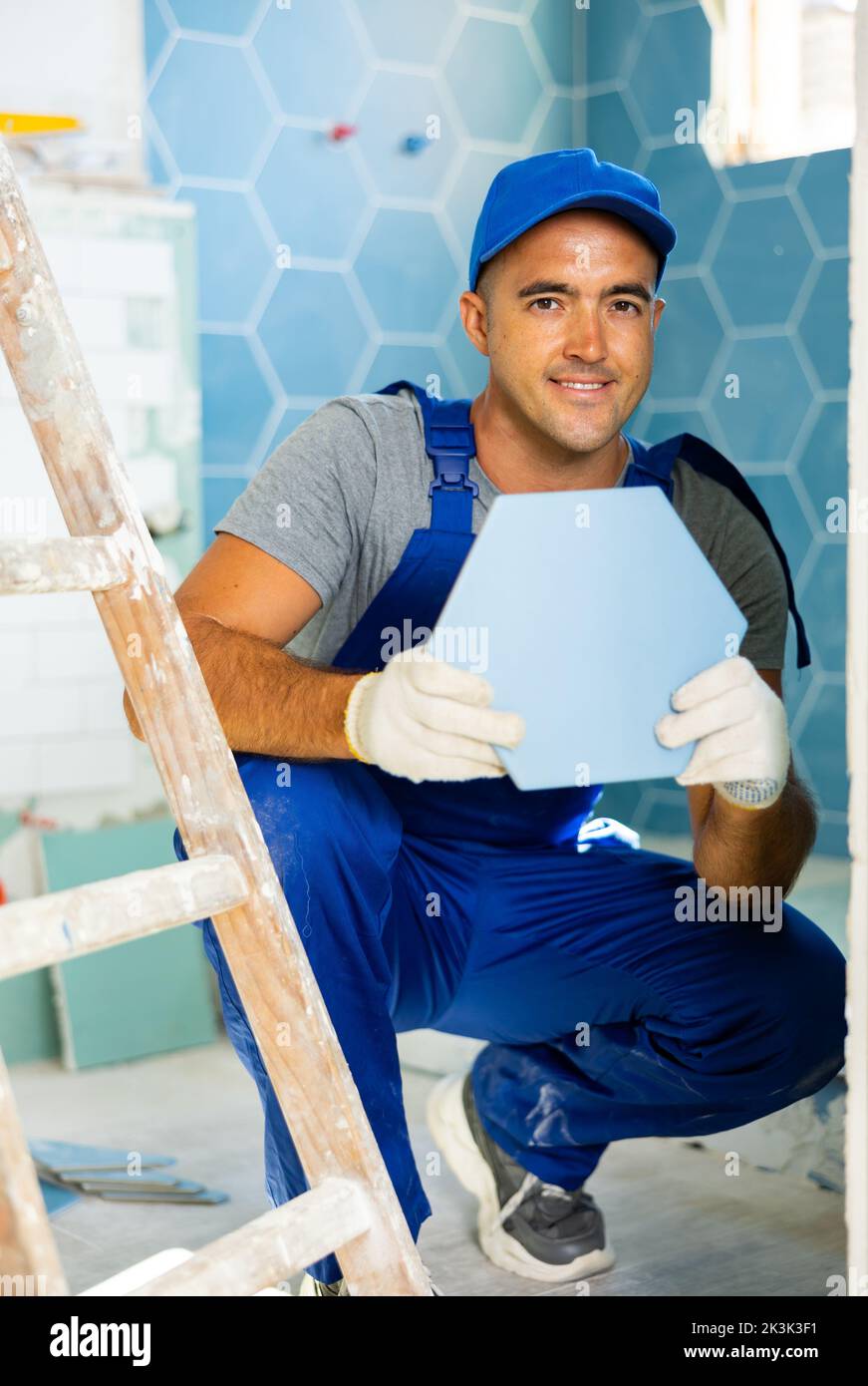 Focused construction worker in work clothes sitting squat engaged in ...