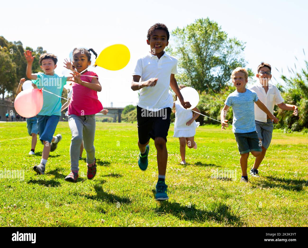 Cheerful kids with balloons are jogging together in the park and having ...