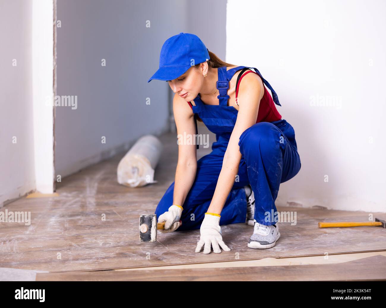 Concentrated woman in blue construction overalls laying laminate ...