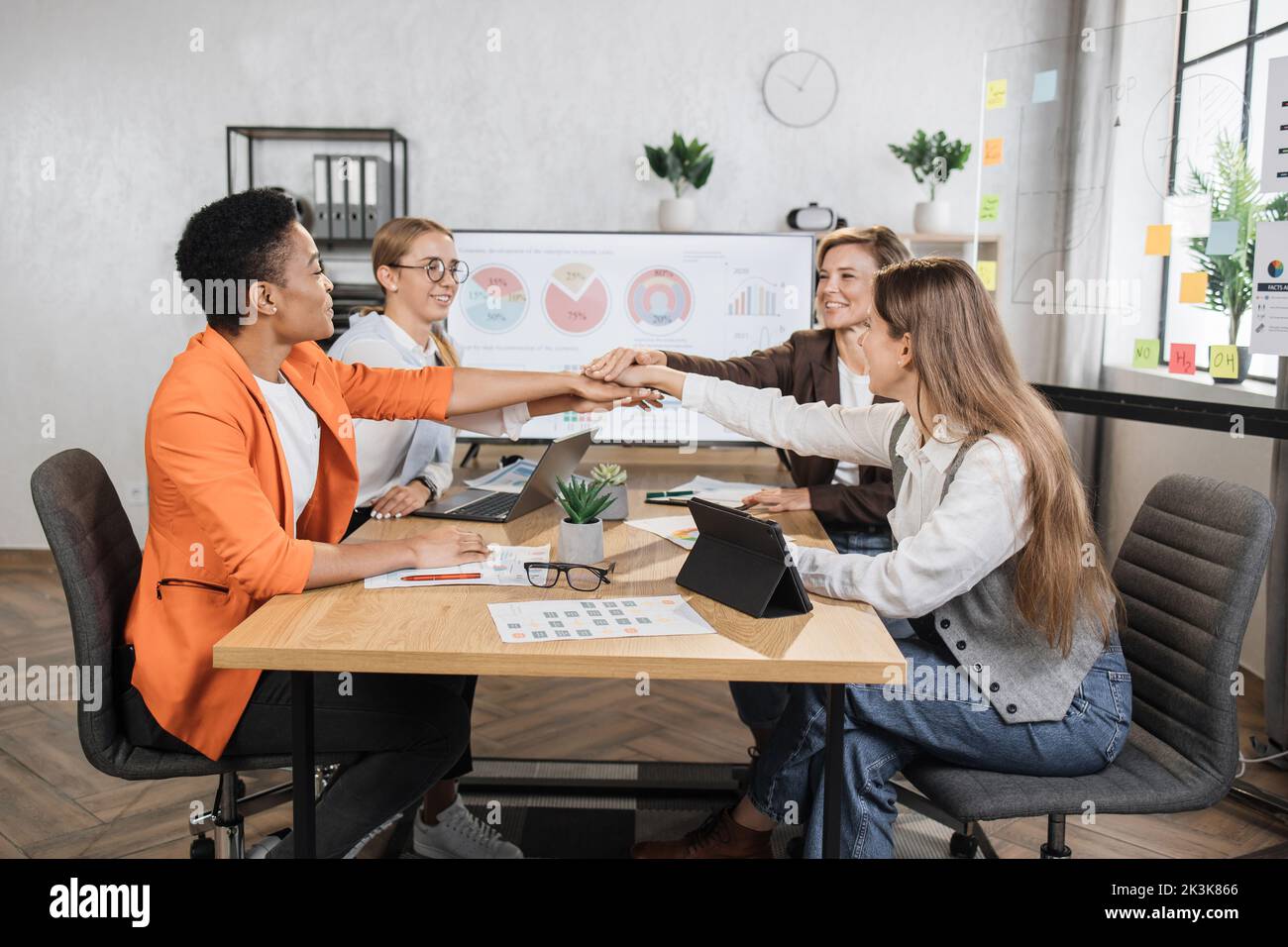 Four happy multiracial female partners stacking their hands together ...