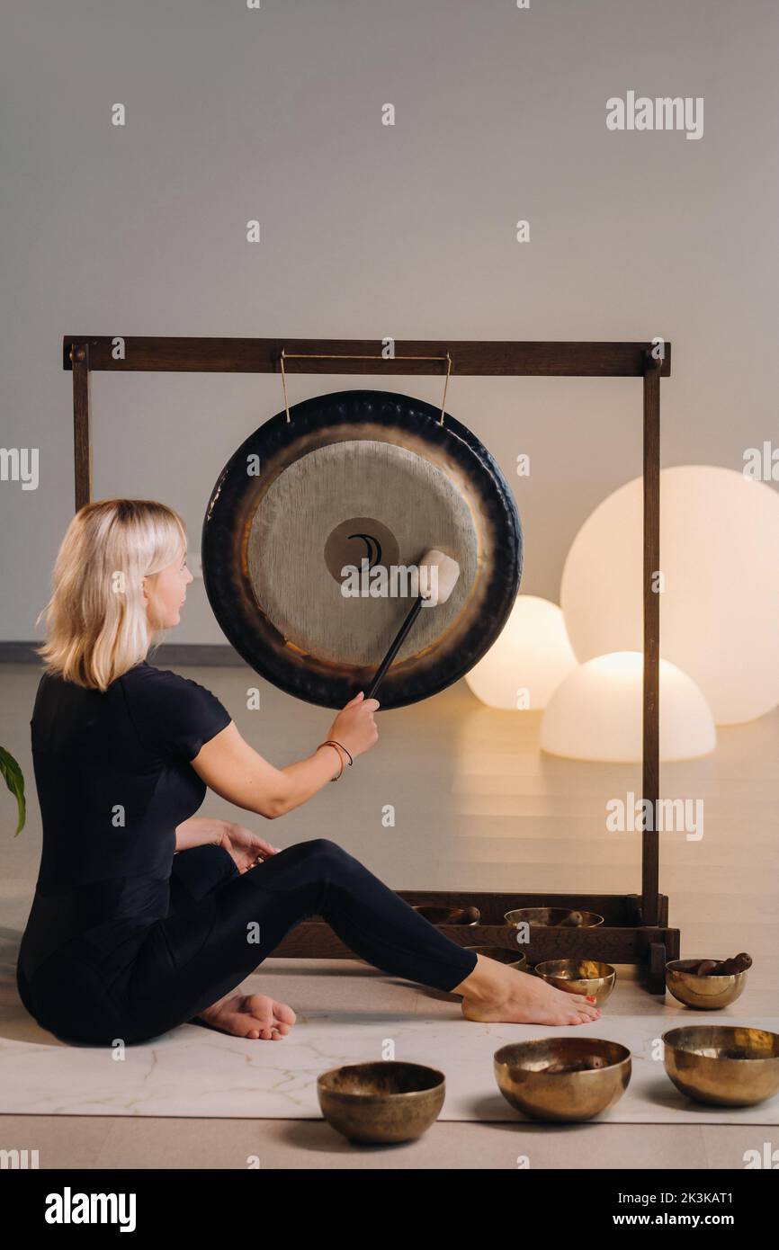 A woman knocks a mallet with a hammer on a gong. A gong and a hand ...