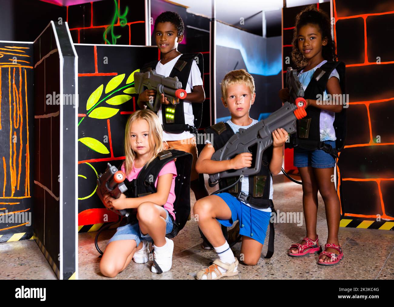 Joyful teens aiming laser guns at other players during lasertag game in ...