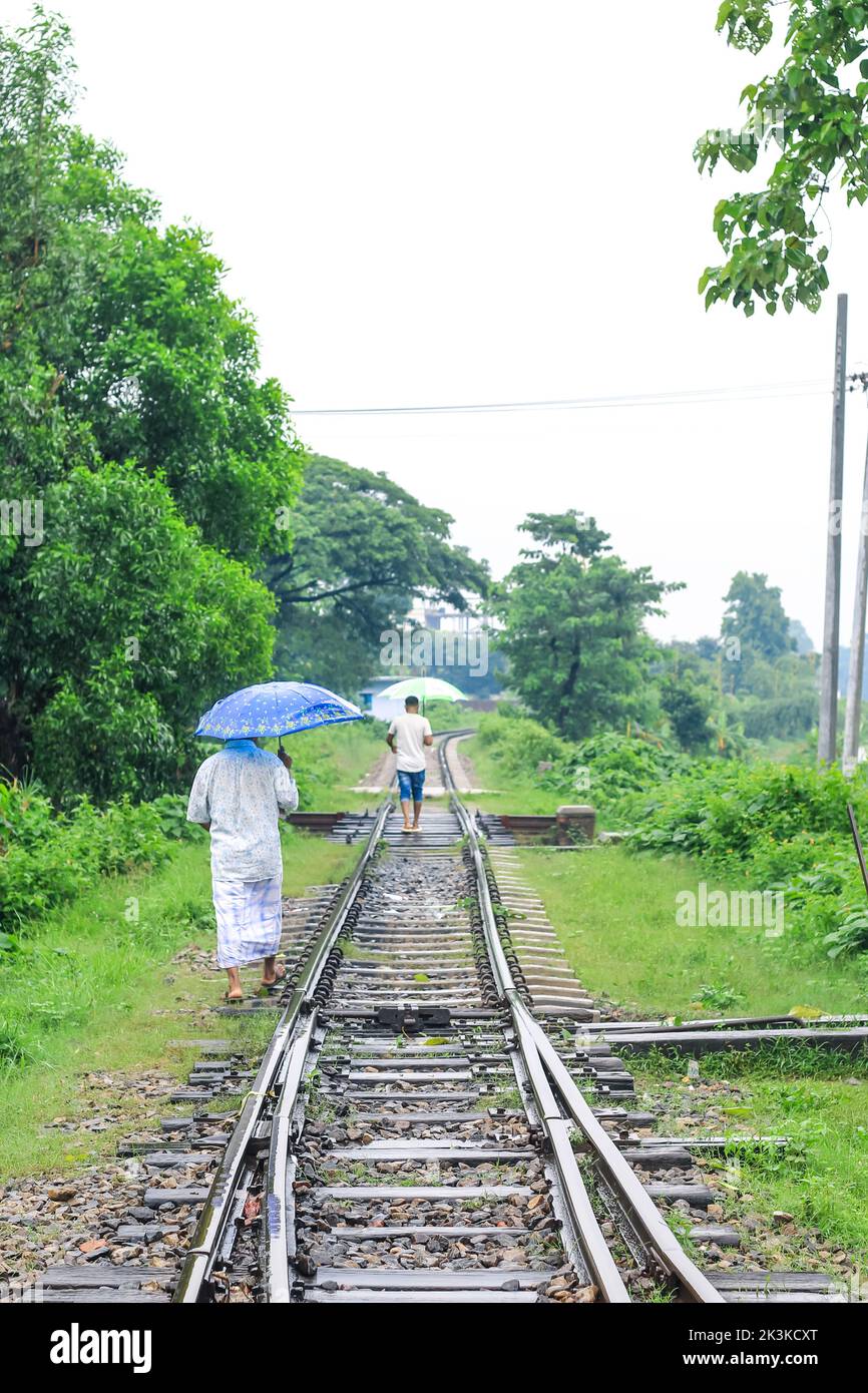 Man walking on the railway on a rainy day. He has an umbrella in his ...