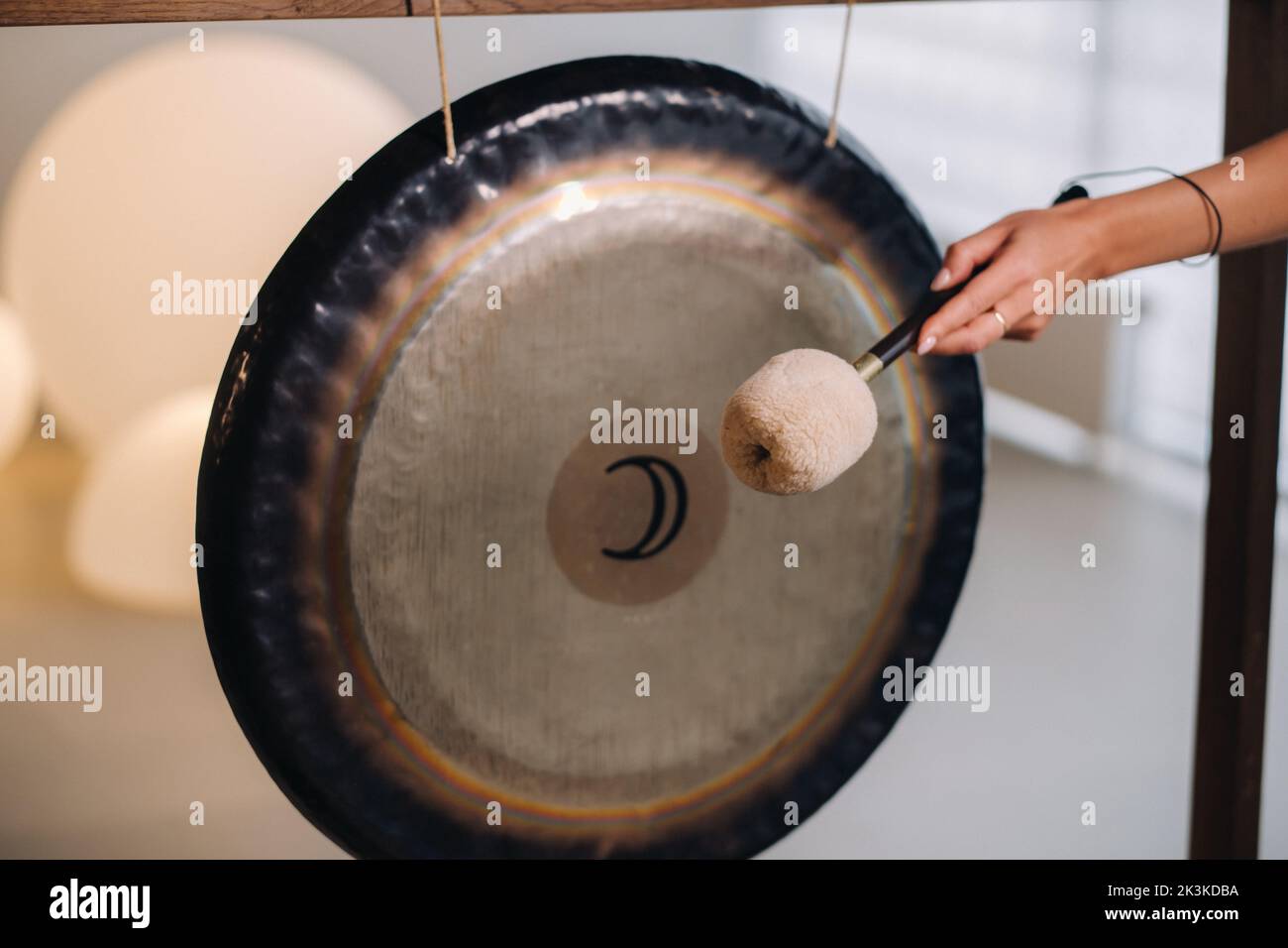 Close-up of a woman's hand pounding a gong with a hammer. Gong and hand ...