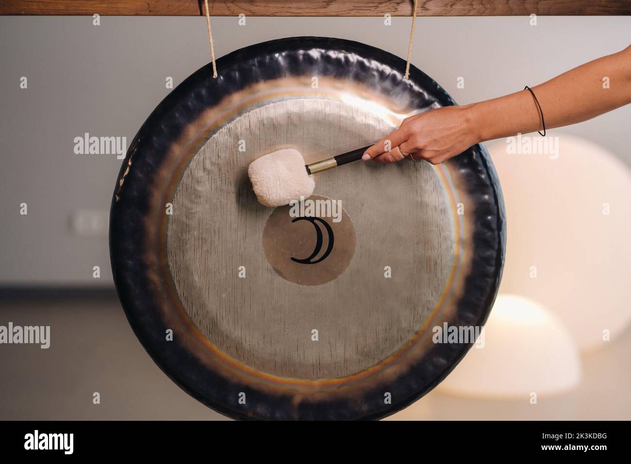 Close-up of a woman's hand pounding a gong with a hammer. Gong and hand ...
