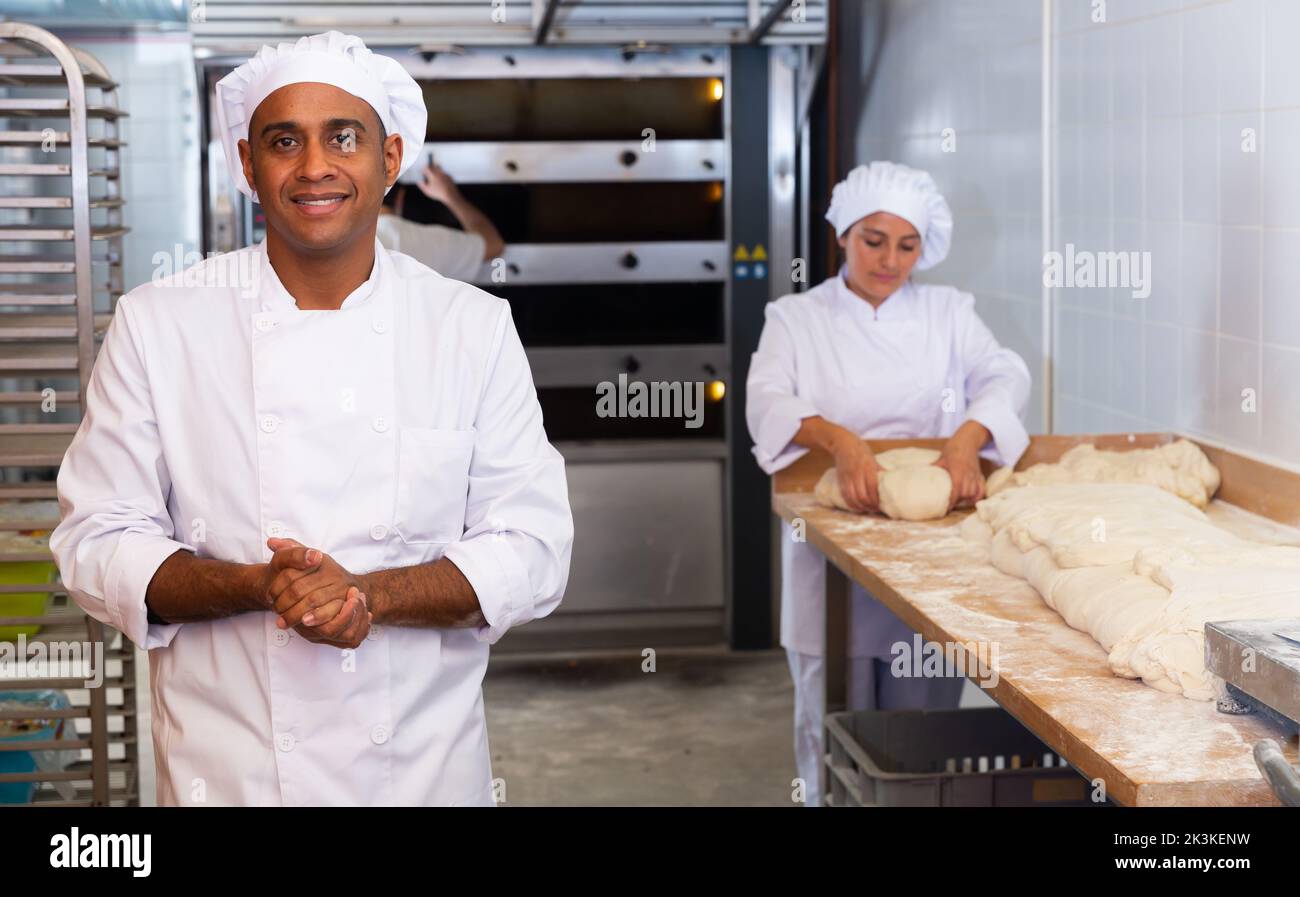 Confident bakery owner posing against busy workers background Stock ...