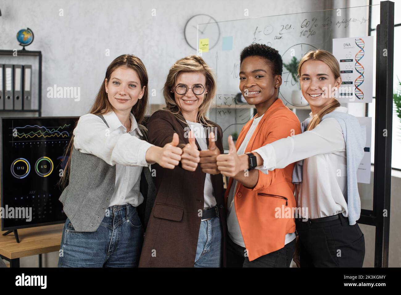 Four multi ethnic female office workers showing thumb up and smiling on camera during business ...