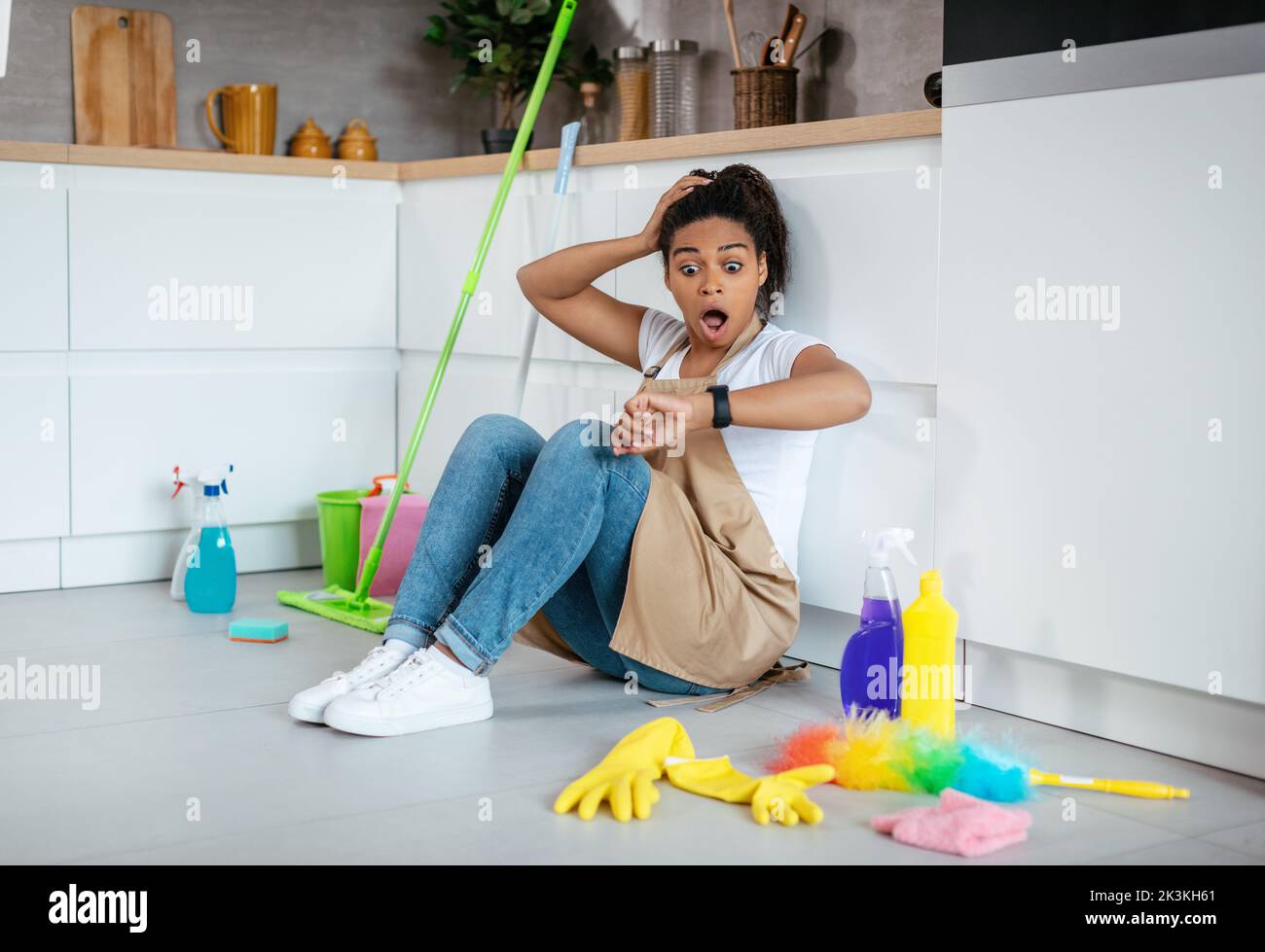 Amazed millennial black lady sits on floor with mop, cleaning supplies ...
