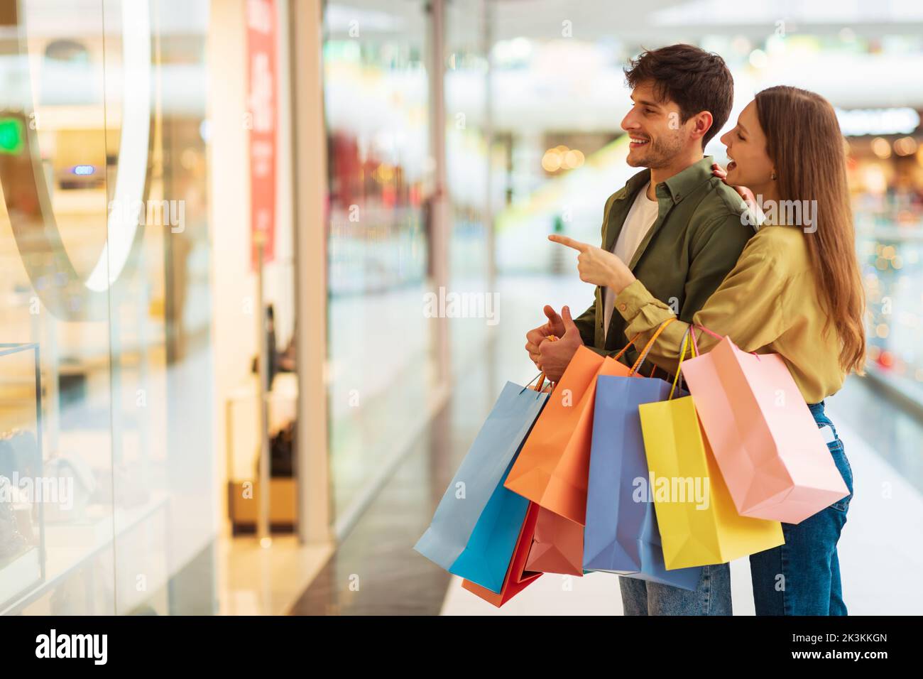 Couple Shopping Pointing Finger At Shop Window In Modern Mall Stock ...
