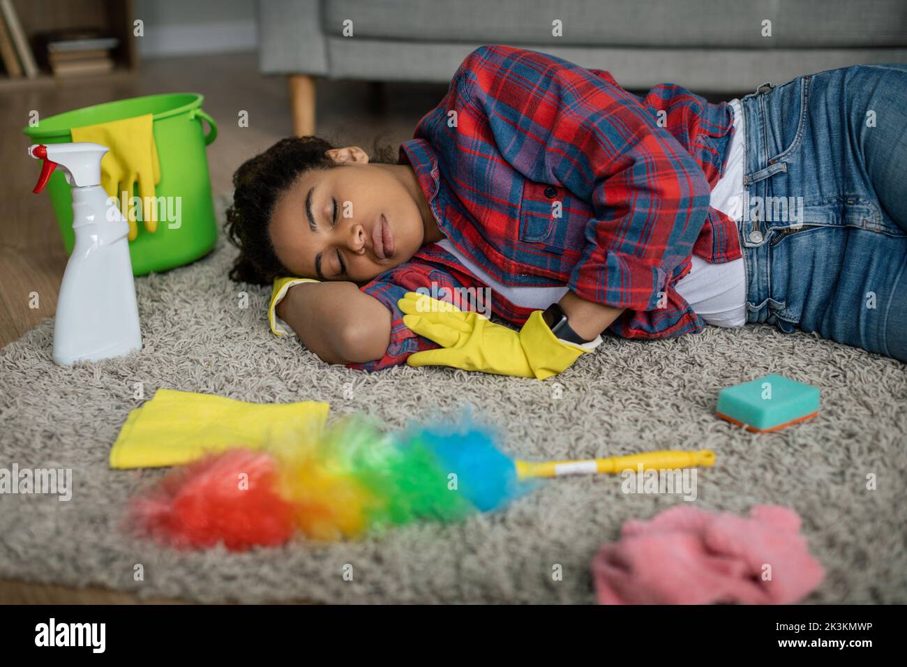 Tired funny young black woman with cleaning supplies sleeping on floor ...