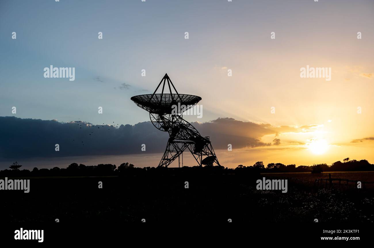 A silhouette shot of a radio telescope dish on a field during sunset ...