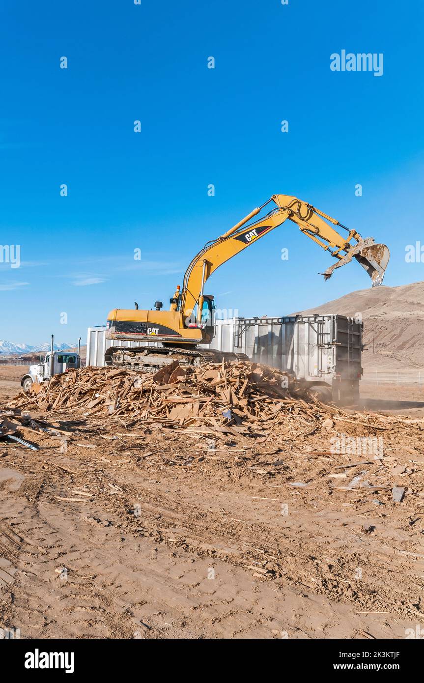 A Caterpillar power shovel sits atop a pile of broken lumber in an ...