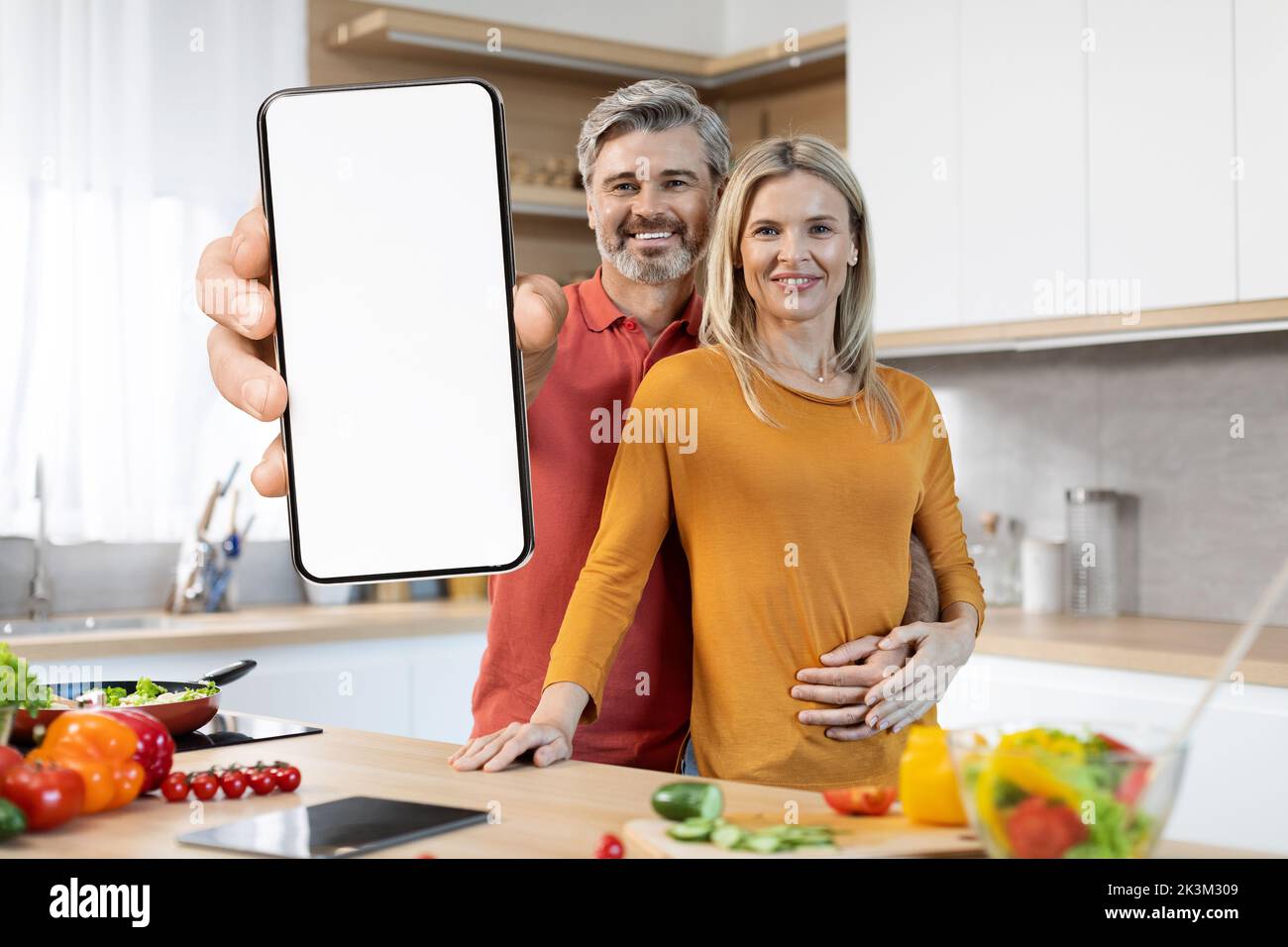 Positive middle aged couple cooking together, showing smartphone ...