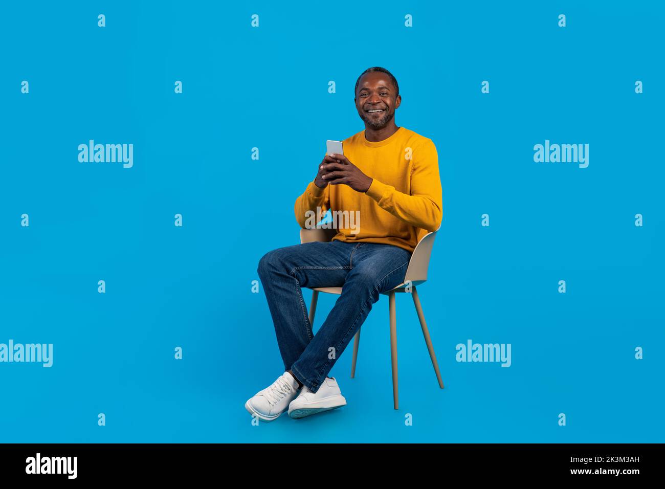 Relaxed black man sitting on chair, using cell phone Stock Photo - Alamy